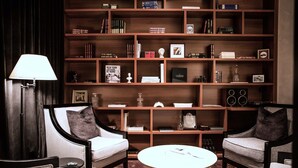 Uma sala de estar acolhedora com estante de livros, duas poltronas, uma mesa de centro redonda e uma luminária.