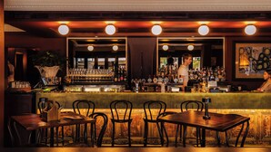 Uma área de bar com balcão, banquetas e um espaço de estar com mesas e cadeiras.