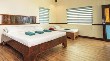 Quarto de hotel com uma cama grande, uma cama menor, piso de madeira e duas janelas com persianas.