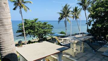 Vista da praia com palmeiras, piscina e um gazebo com vista para o oceano.