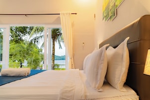 Quarto de hotel com cama, vista para áreas verdes e água, e cortina.