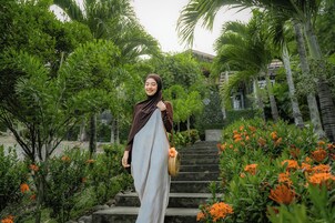 Uma mulher caminhando em uma escadaria rodeada por vegetação exuberante e flores laranjas.
