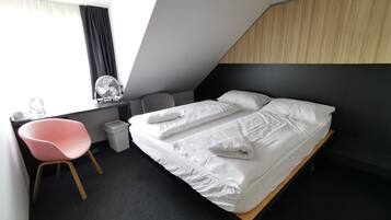 Quarto de hotel moderno com cama, escrivaninha, cadeira e janela com cortinas.