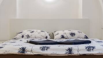 Uma cama com colcha estampada em flor e duas almofadas, cabeceira e parede com luminária.