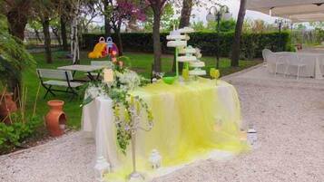 Montagem de casamento ao ar livre com mesa coberta, cadeiras e arranjo floral.