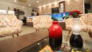 Um hall de hotel com sofás estampados, uma mesa de recepção e uma mesa de centro de vidro com objetos decorativos.