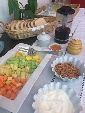 Um buffet de café da manhã com diversas frutas, uma cafeteira e um pote de mel.