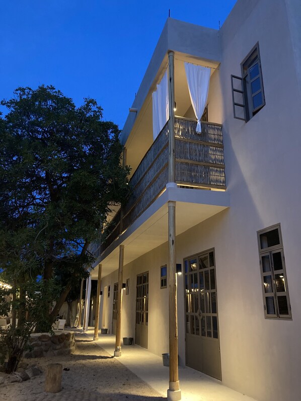 Um edifício de dois andares com uma varanda, janelas amplas e uma árvore em primeiro plano.