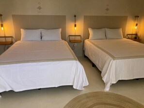 Duas camas de solteiro com roupa de cama branca e cabeceiras, mesas de cabeceira com abajures e um tapete em tons neutros.