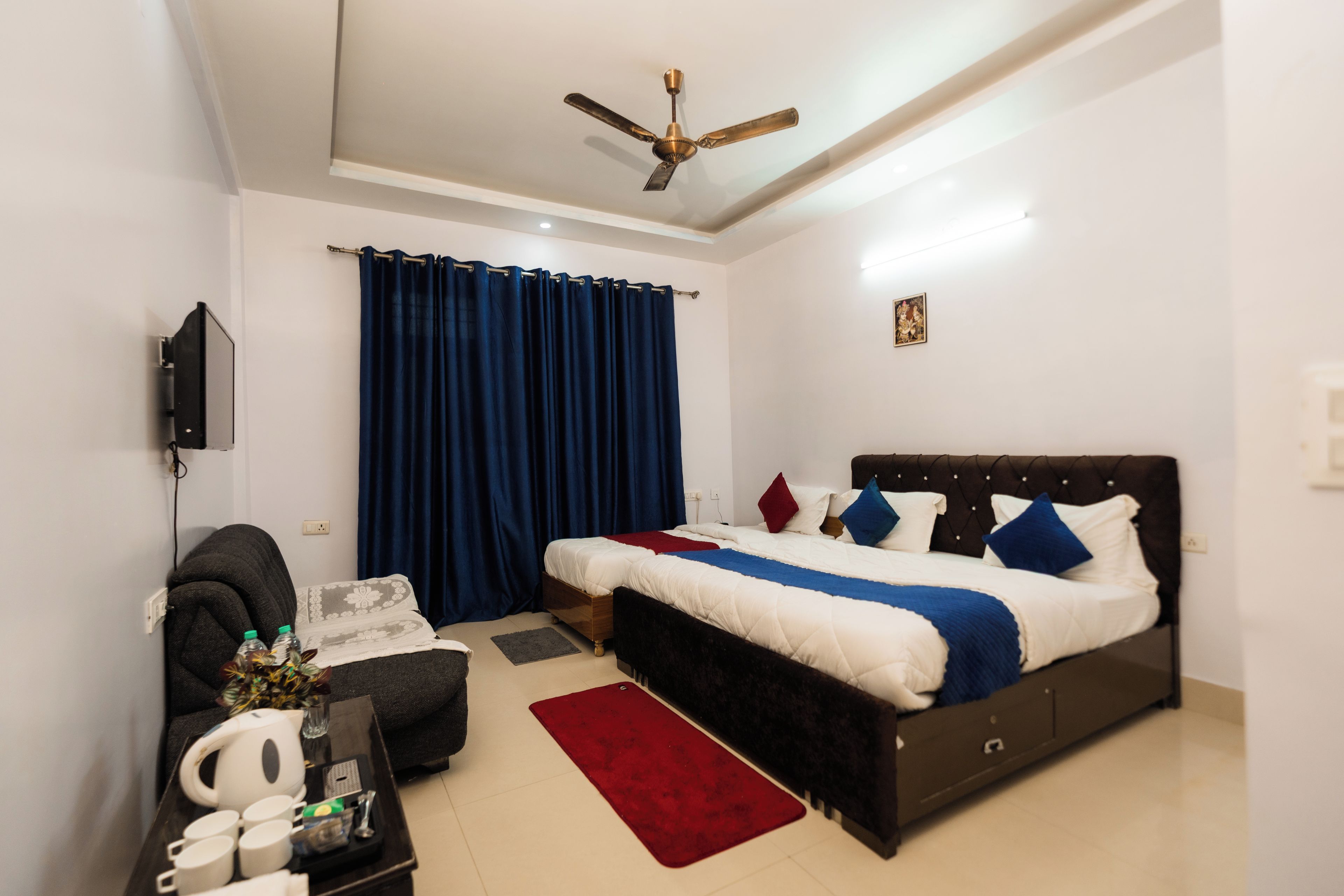 Quarto de hotel com cama, escrivaninha, cadeira, televisão e ventoinha no teto.