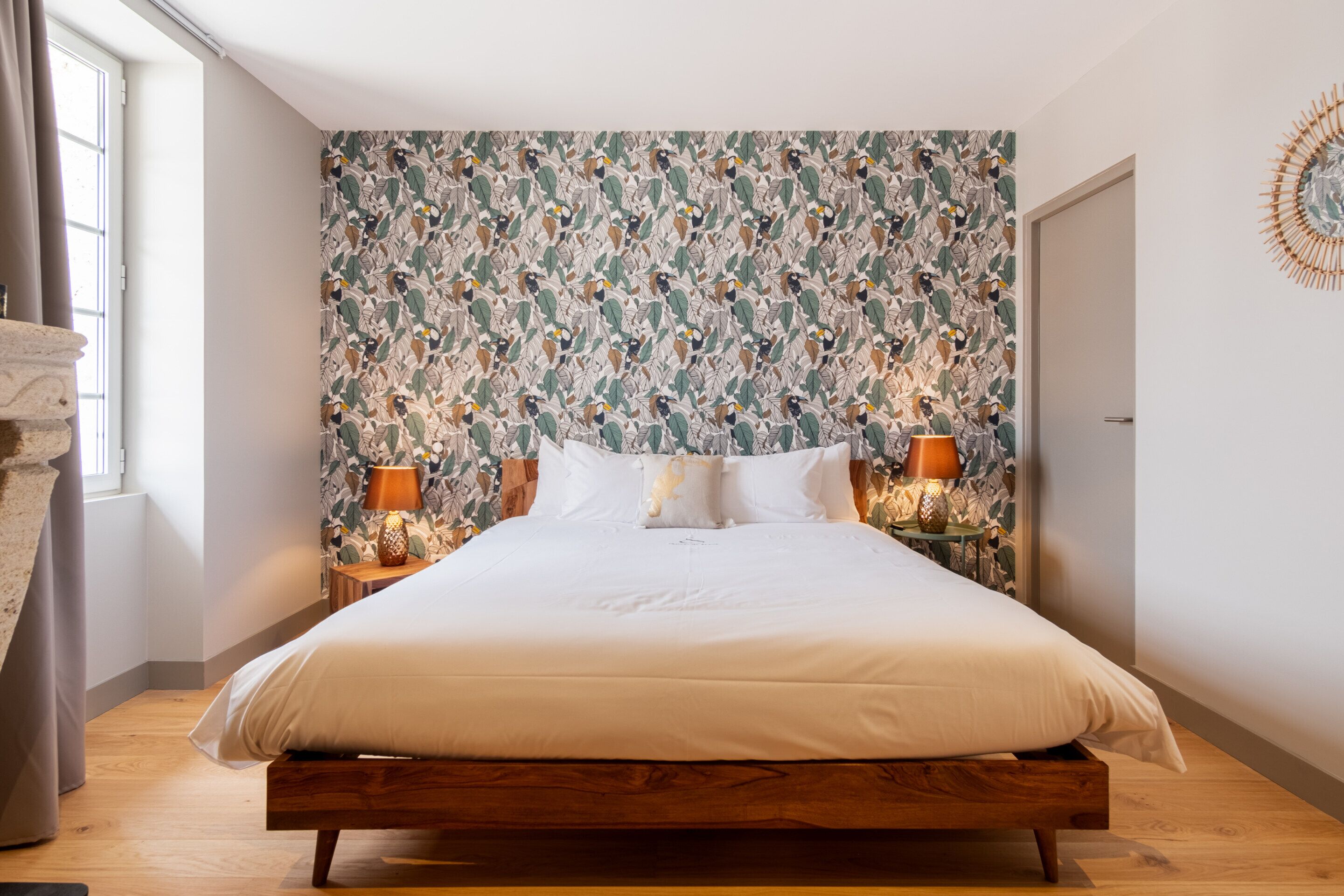 Quarto com cama grande, papel de parede floral, duas luminárias de cabeceira e lareira de pedra.