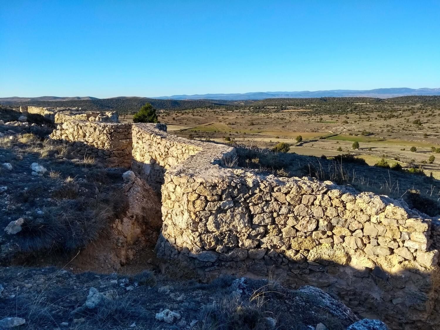 Paredes de pedra com vista para uma paisagem rural ao fundo.
