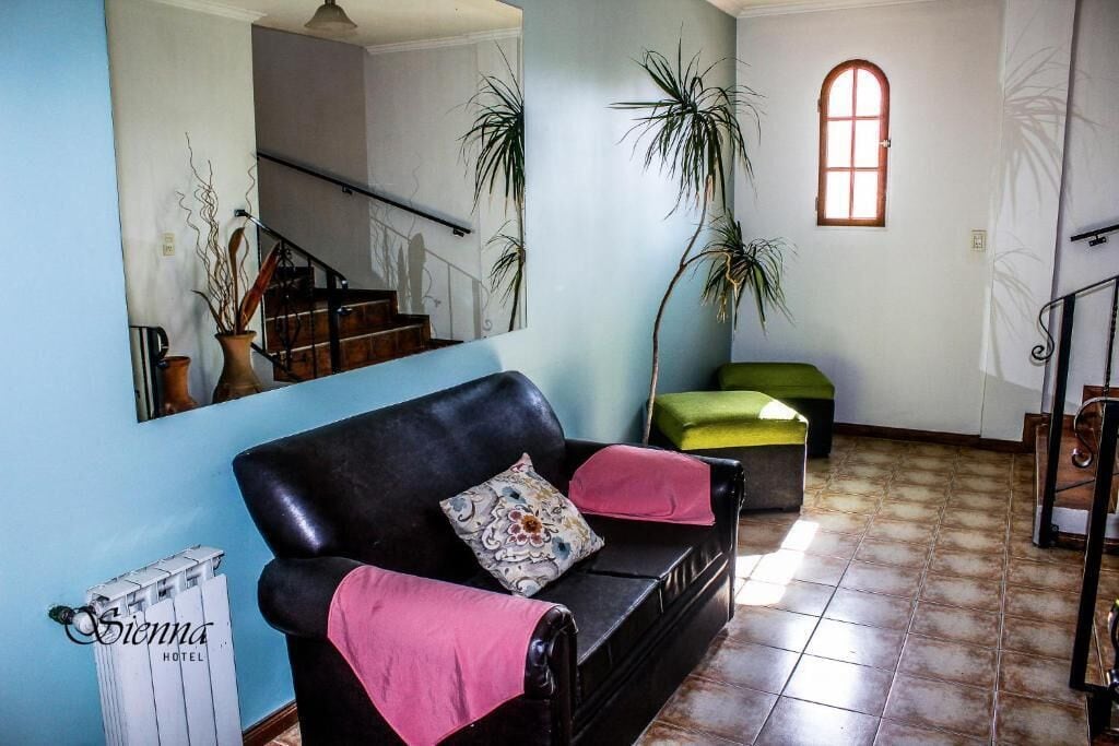 Um saguão de hotel com um sofá de couro preto, um banquinho verde e uma escada.