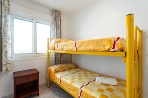 Quarto com beliche, mesa de cabeceira de madeira e janela com cortinas.