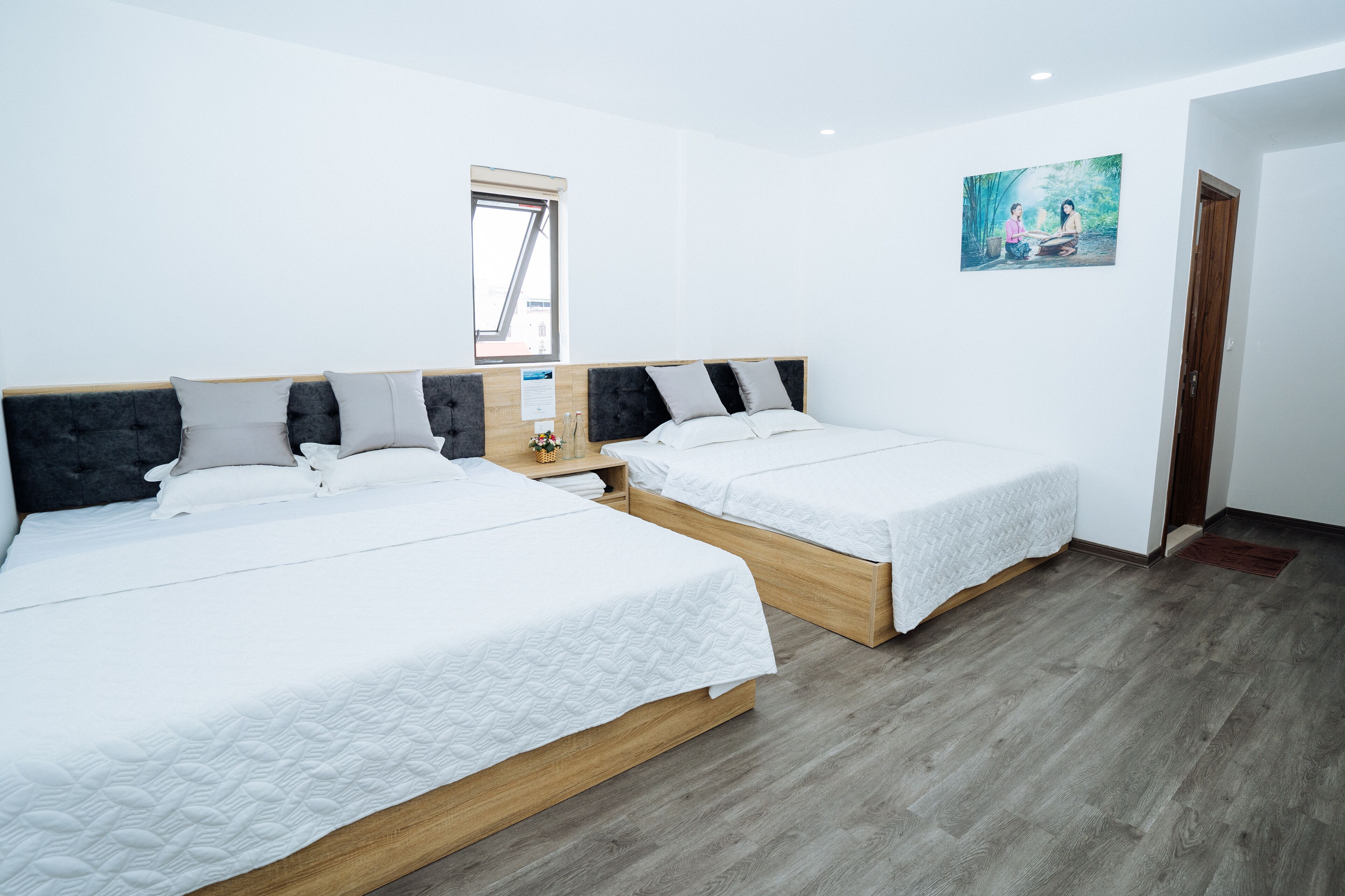 Quarto de hotel com duas camas, uma janela, um quadro e chão de madeira.