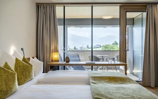 Quarto de hotel com uma cama, uma escrivaninha e vista para a cidade através de grandes janelas.