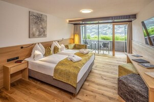 Quarto de hotel com cama, escrivaninha, cadeira e varanda com vista para o campo.