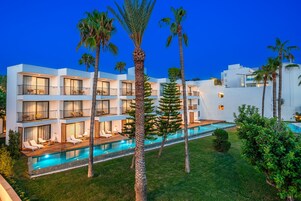 Hotel com várias varandas, piscina e palmeiras.