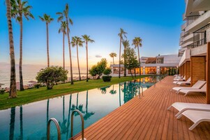 Uma piscina com um deck de madeira, cadeiras de espreguiçadeira e palmeiras.