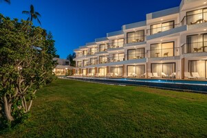 Um hotel moderno com piscina, várias varandas e um jardim bem cuidado.