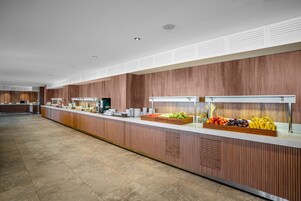 Uma área de buffet com um balcão longo, painéis de madeira e diversas opções de comida.