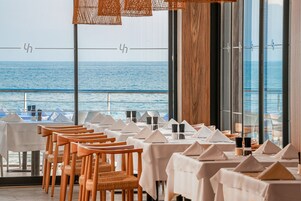 Uma área de refeições com mesas preparadas para o serviço, com vista para o mar.
