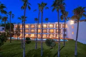 Hotel de vários andares com piscina, rodeado por palmeiras e gramados bem cuidados.