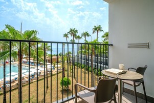 Uma varanda com vista para uma área de piscina, palmeiras e um edifício com varandas.