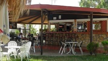 Um café ao ar livre com mesas, cadeiras, um muro de pedra e uma área de estar coberta.