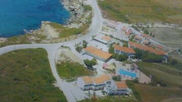Vista aérea de uma estância costeira com uma estrada sinuosa, vários edifícios e uma piscina.