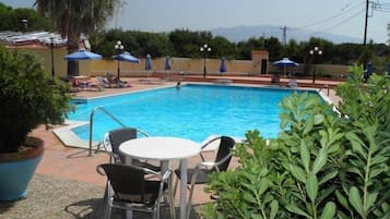 Piscina cercada por vegetação, com espreguiçadeiras e guarda-sóis.