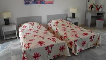 Quarto de hotel com duas camas de solteiro, uma escrivaninha, uma cadeira, mesa de cabeceira, luminária e espelho.