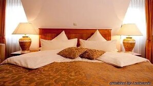 Quarto de hotel com uma cama grande, duas luminárias de cabeceira e uma cabeceira de madeira.