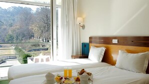 Quarto de hotel com duas camas, vista para uma floresta e itens de café da manhã sobre as camas.