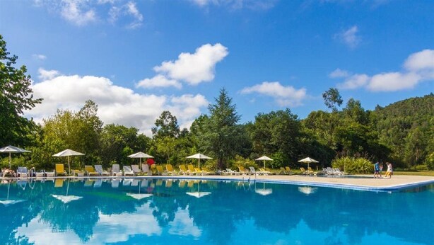 Piscina com espreguiçadeiras e guarda-sóis, cercada por árvores e um céu claro.