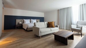 Quarto de hotel moderno com cama, sofá, mesa de centro e uma cadeira.