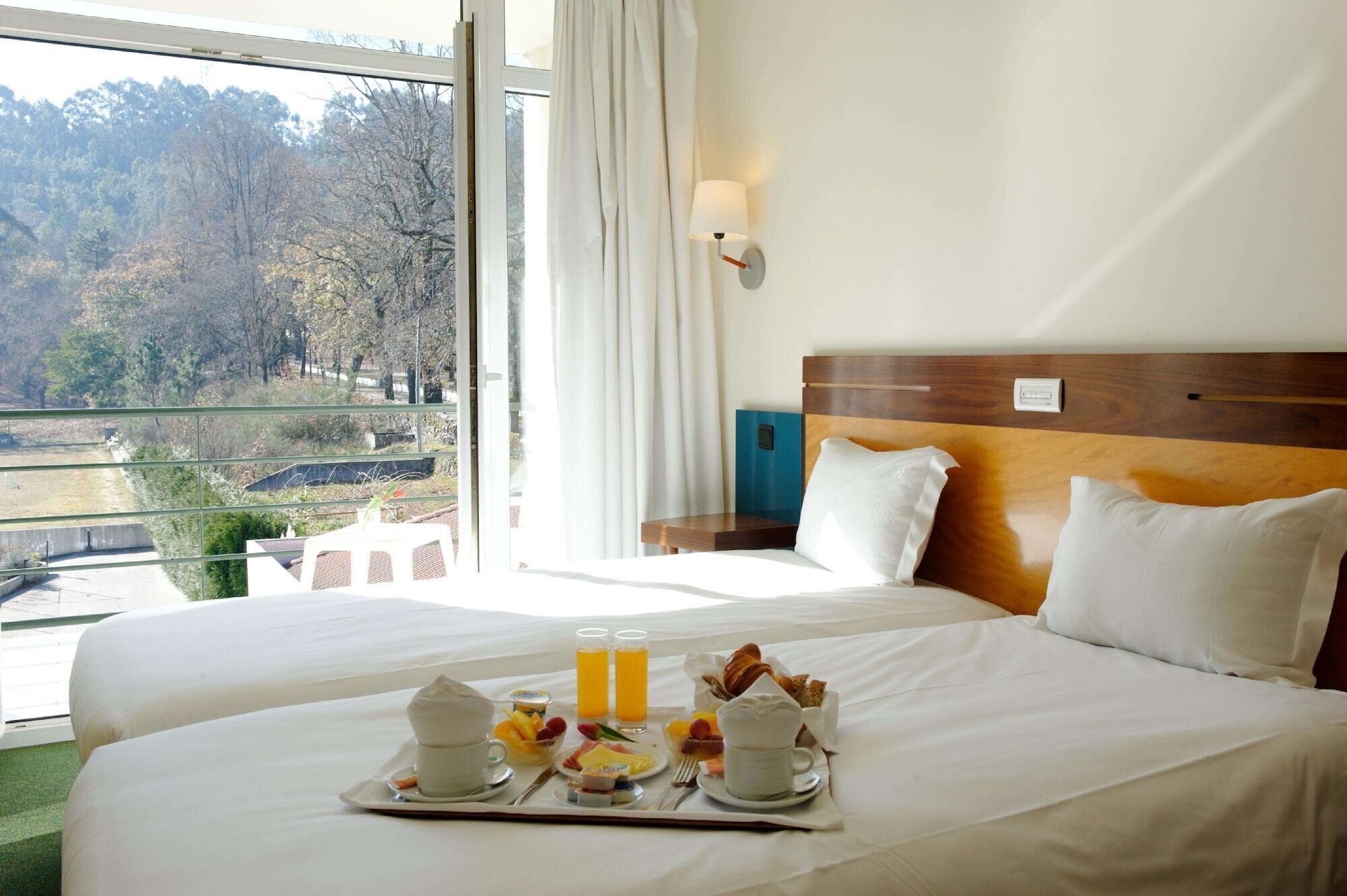 Quarto de hotel com uma cama grande, uma mesinha de cabeceira e vista para uma floresta pela janela.