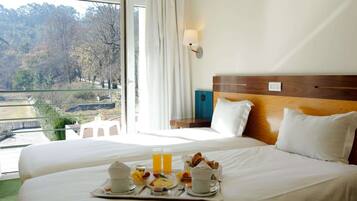 Quarto de hotel com uma cama grande, uma mesinha de cabeceira e vista para uma floresta pela janela.