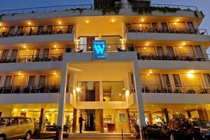 Um hotel com vários andares, varandas, uma placa 'W' em destaque e uma entrada bem iluminada.