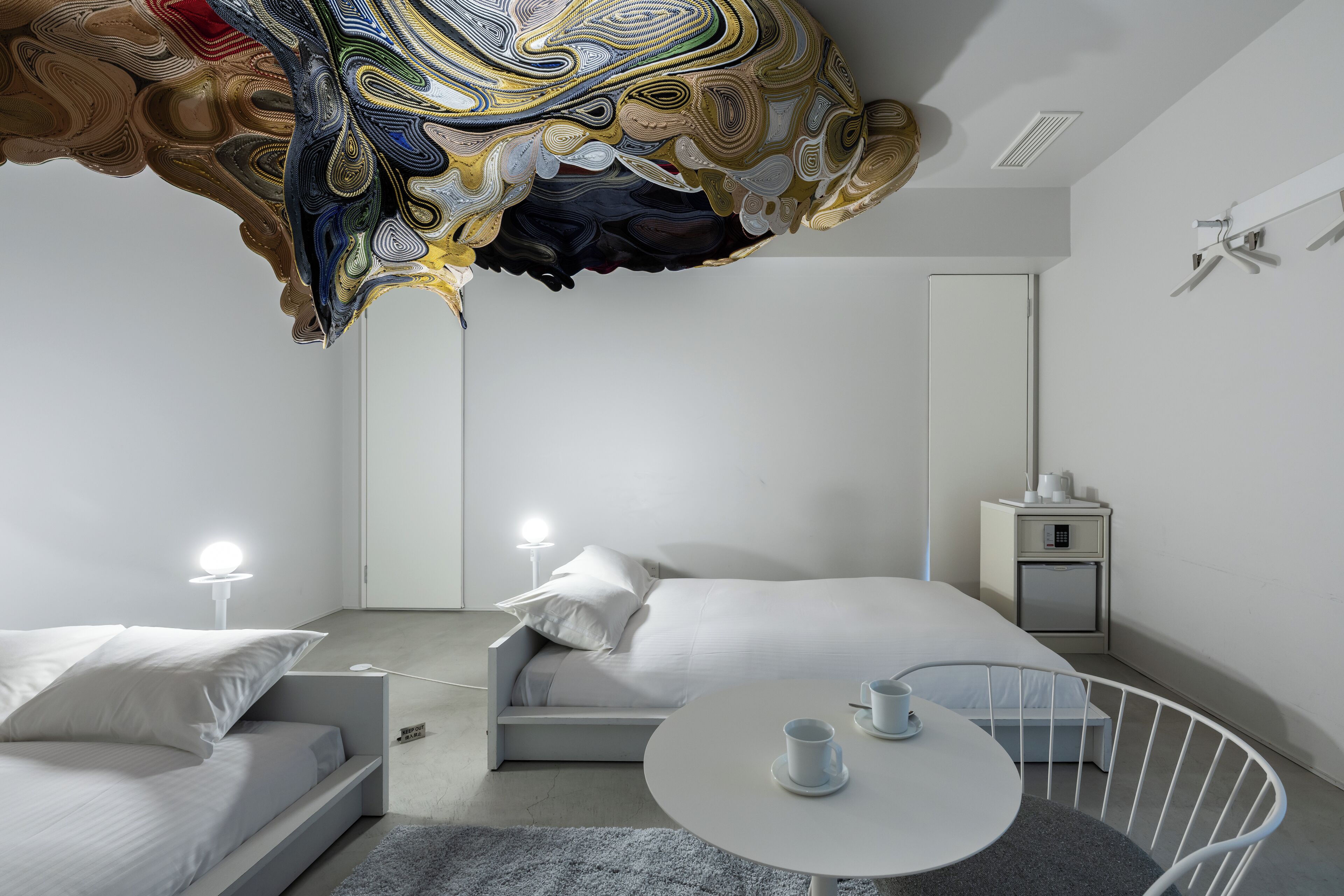 Quarto de hotel moderno com cama, mesa de cabeceira e uma pequena mesa redonda com chávenas.