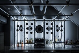 Uma área de bar com um alto-falante central e várias garrafas de bebidas alcoólicas nas prateleiras.