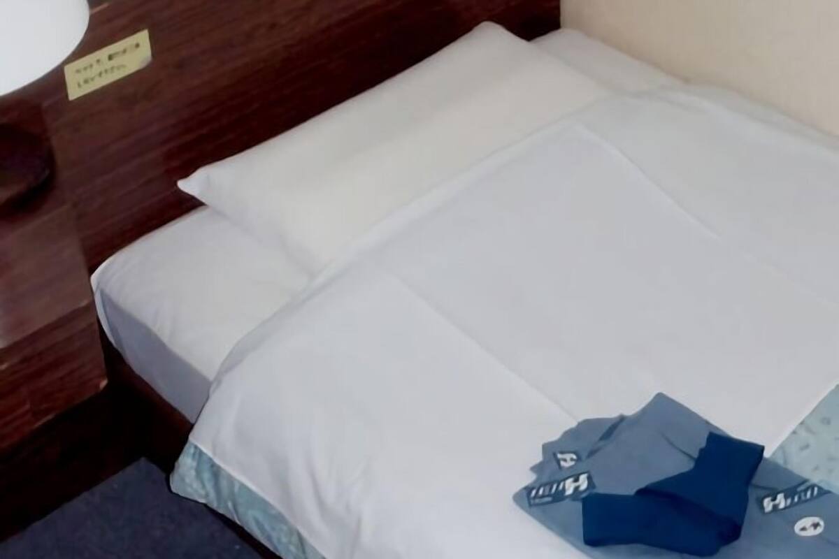 Cama bem arrumada com lençóis brancos, cabeceira de madeira e uma pequena mesa de cabeceira com abajur.