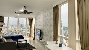 Uma sala de estar moderna com uma janela ampla, um ventilador de teto, uma televisão de tela plana, um sofá, uma mesa de centro e um espaço de jantar com uma mesa e cadeiras brancas.