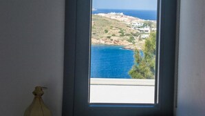 Janela com vista para paisagem costeira, um pequeno candeeiro e uma fileira de livros numa estante.