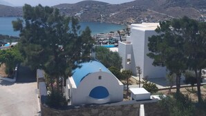 Vista costeira com um edifício branco com cúpula azul, rodeado por árvores e céu claro.