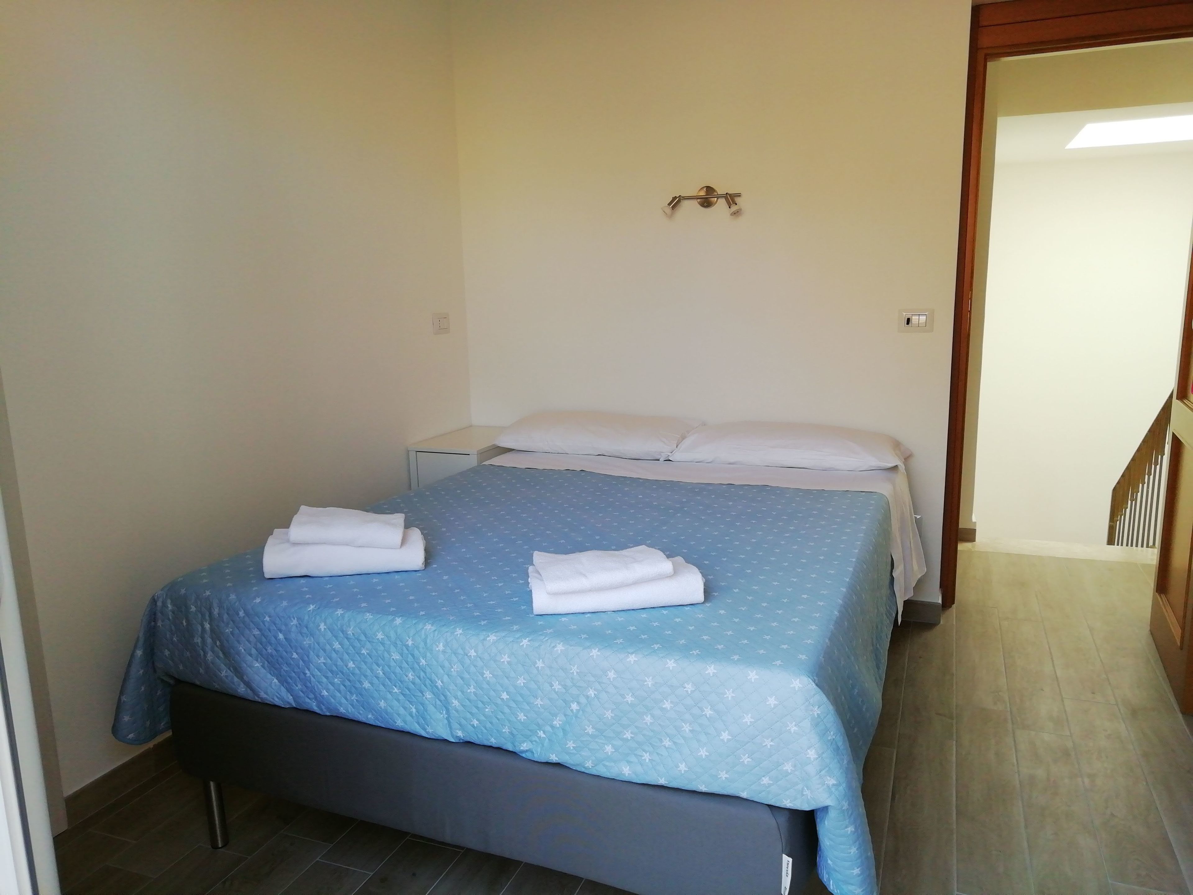 Quarto com cama, duas mesas de cabeceira e luminária fixada na parede.
