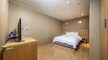 Quarto de hotel com escrivaninha de madeira, cama com roupa de cama branca e cabeceira.