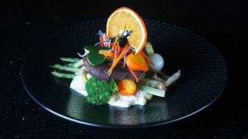 Um prato negro com diversos alimentos, incluindo um pedaço de carne, legumes e uma fatia de laranja.
