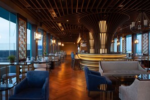 Interior moderno de restaurante com balcão curvo, piso de madeira e amplas janelas com vista para a cidade.