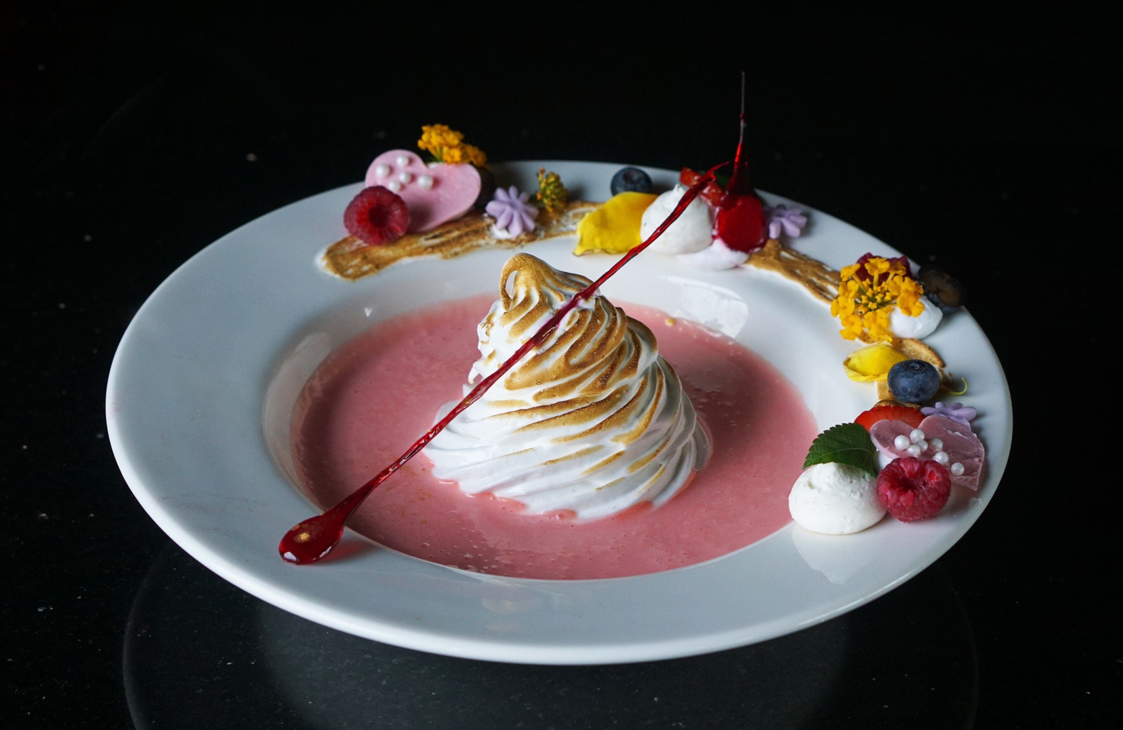 Prato de sobremesa com merengue, chantilly e diversas frutas e flores.